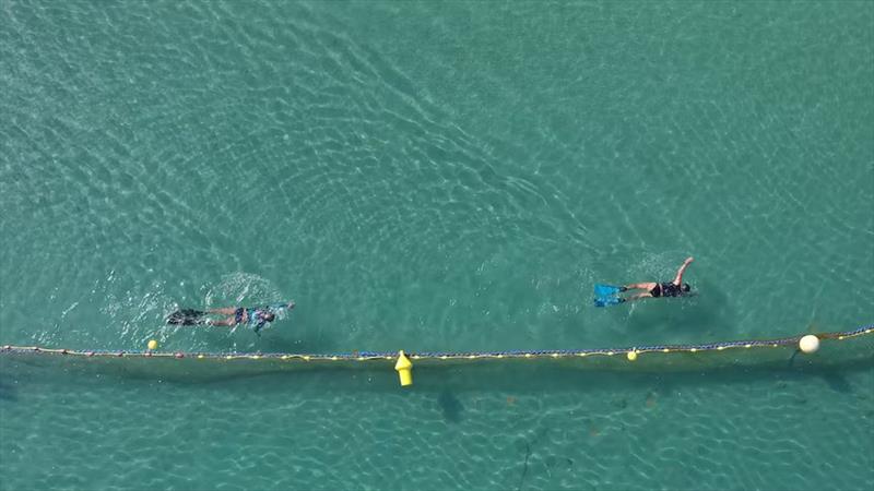 Two swimmers swim along a roped-off area at a beach in New Caledonia